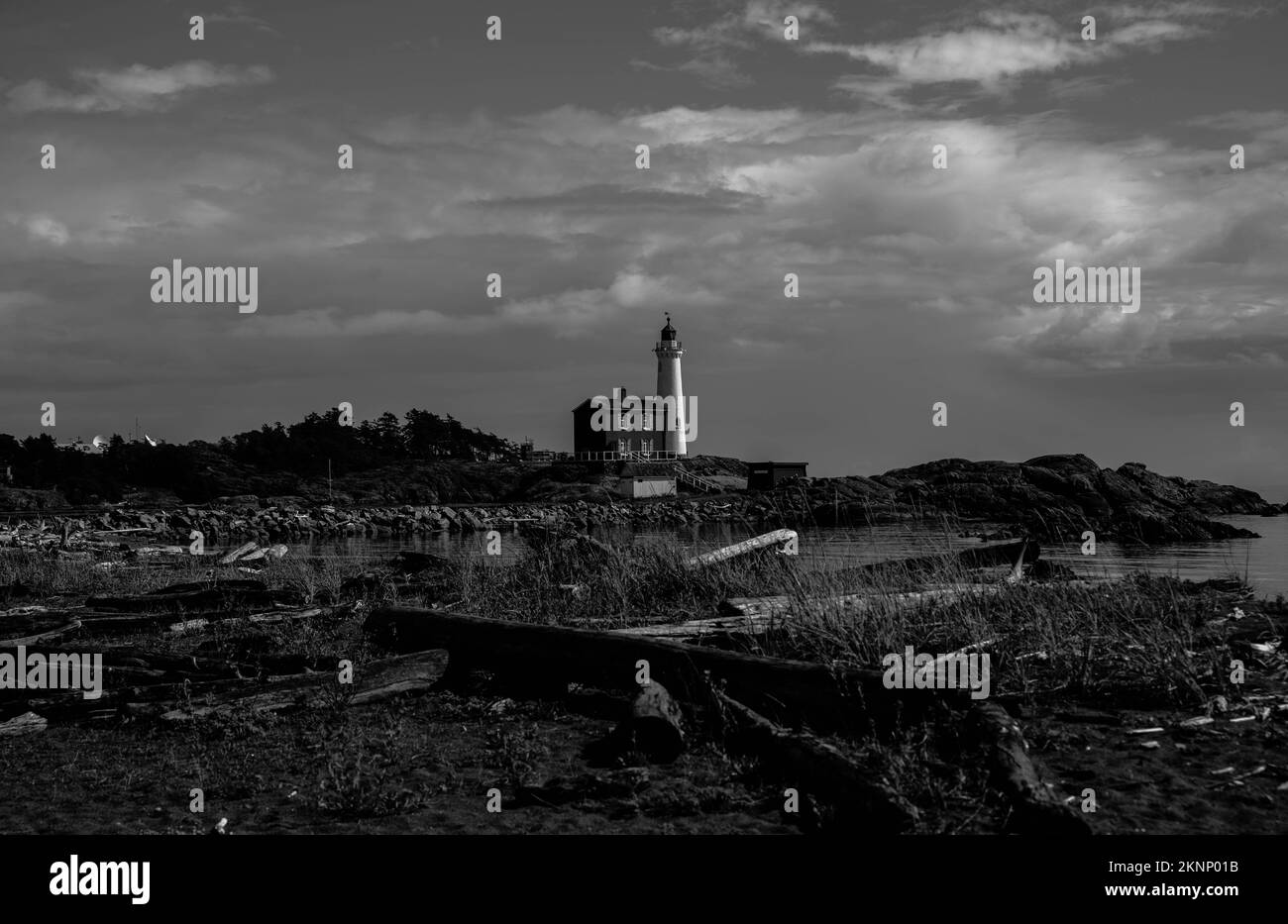 A greyscale shot of a small lighthouse building built by the shore of a ...