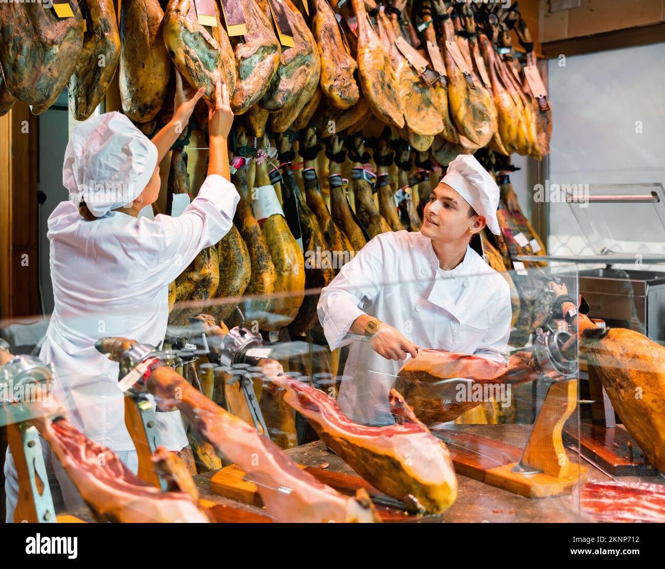 Young female and male vendors arranging jamon at counter in butcher ...