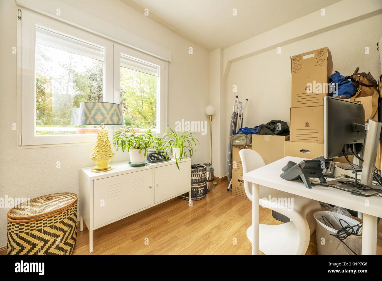 A cluttered room with white furniture and a window overlooking a garden ...