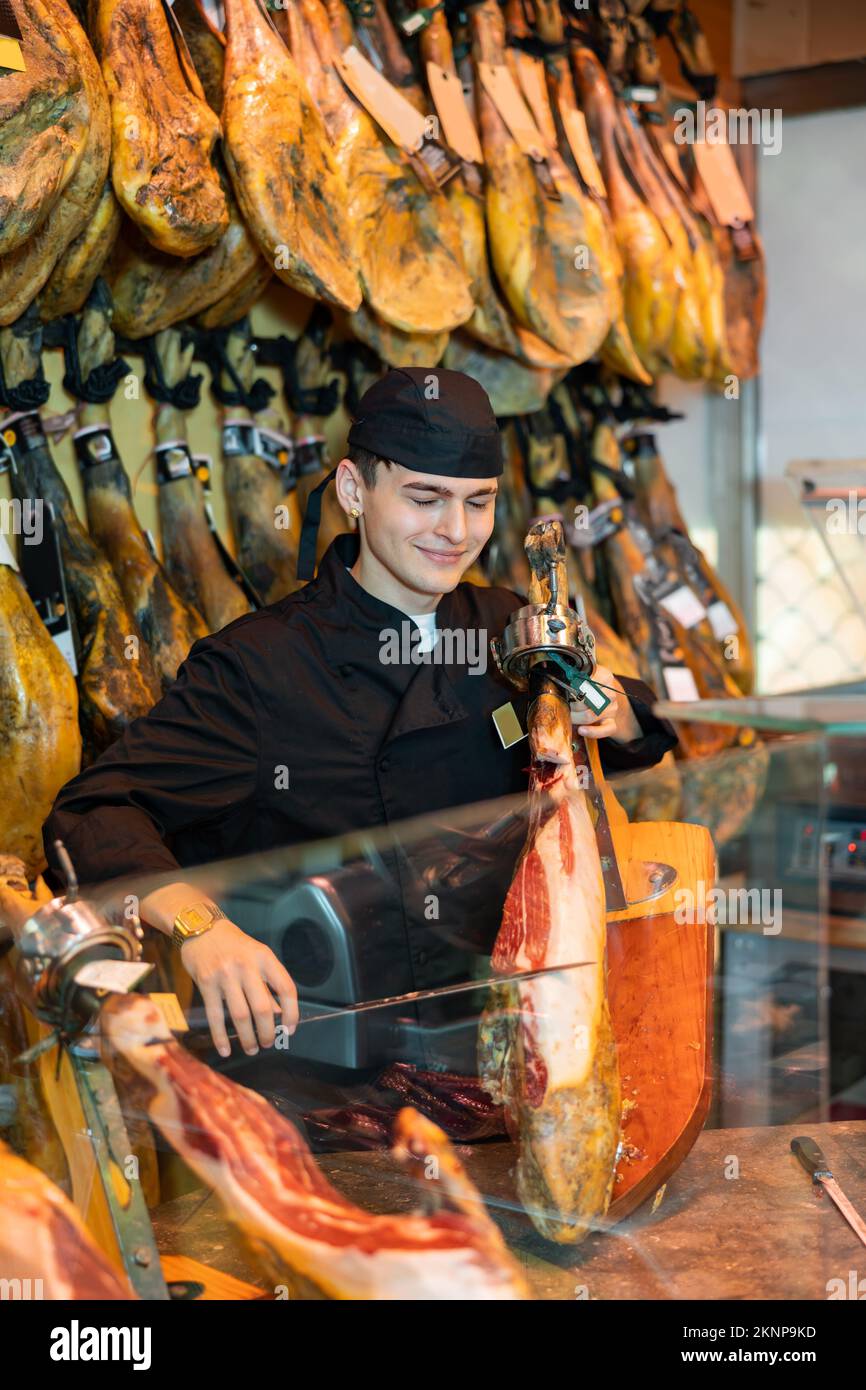 Positive young man carving jamon slices from pig's leg Stock Photo - Alamy
