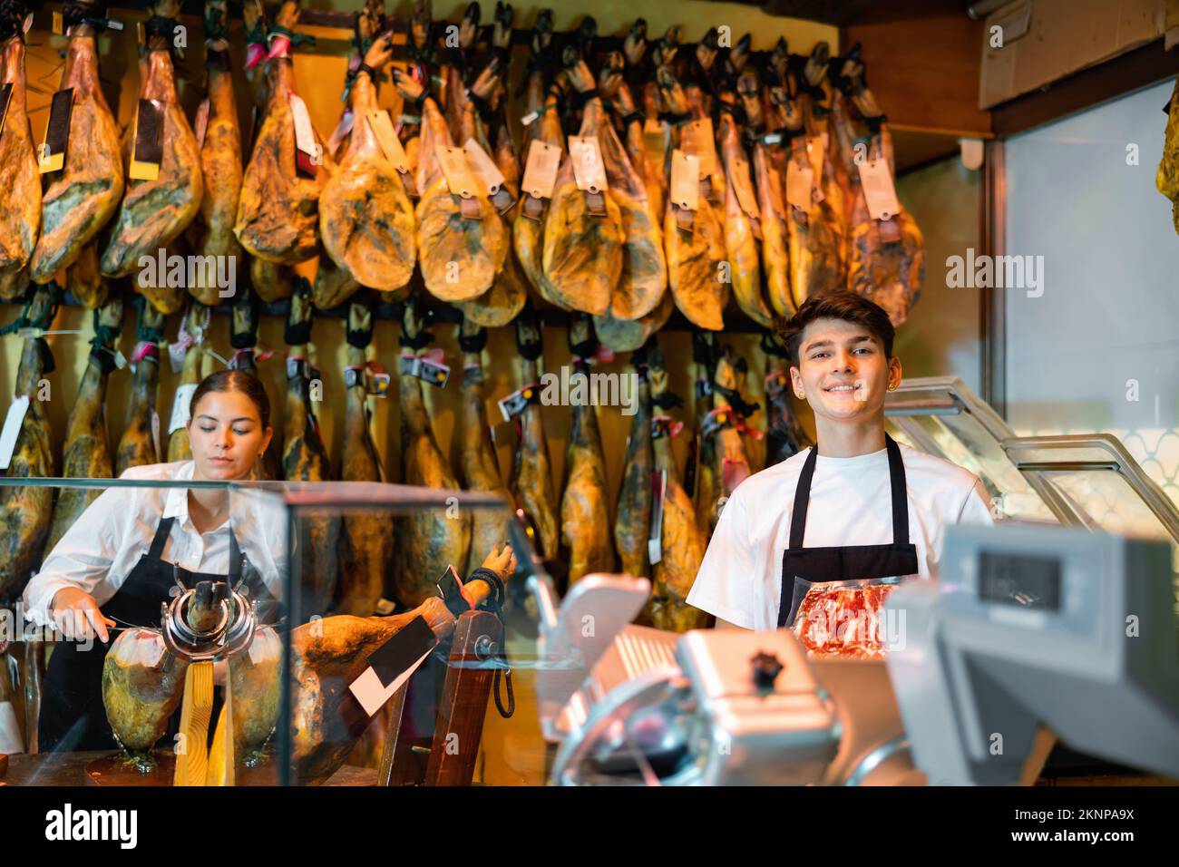Young female and male vendors arranging jamon at counter in butcher ...
