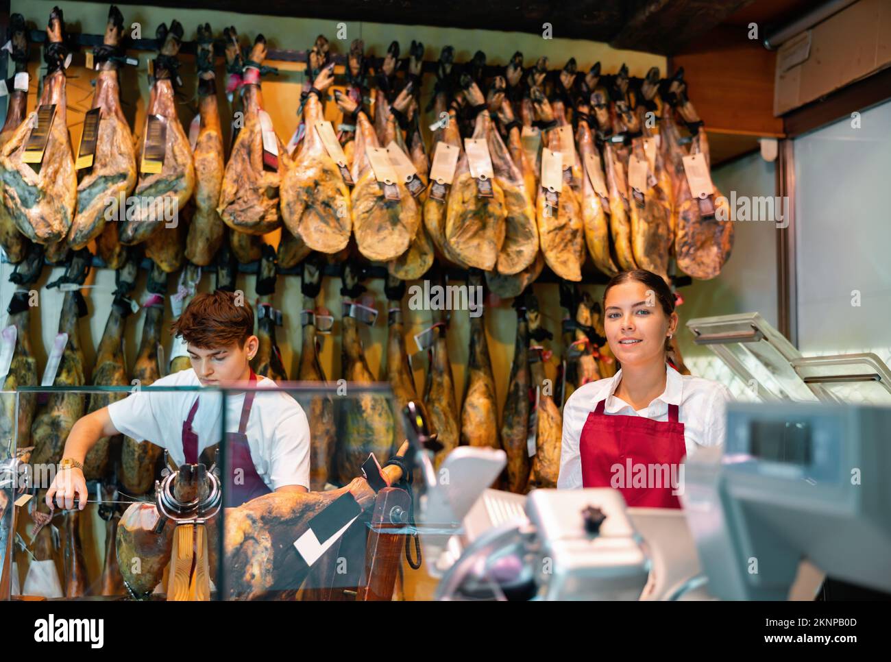 Positive young man and woman selling spanish jamon at counter Stock ...