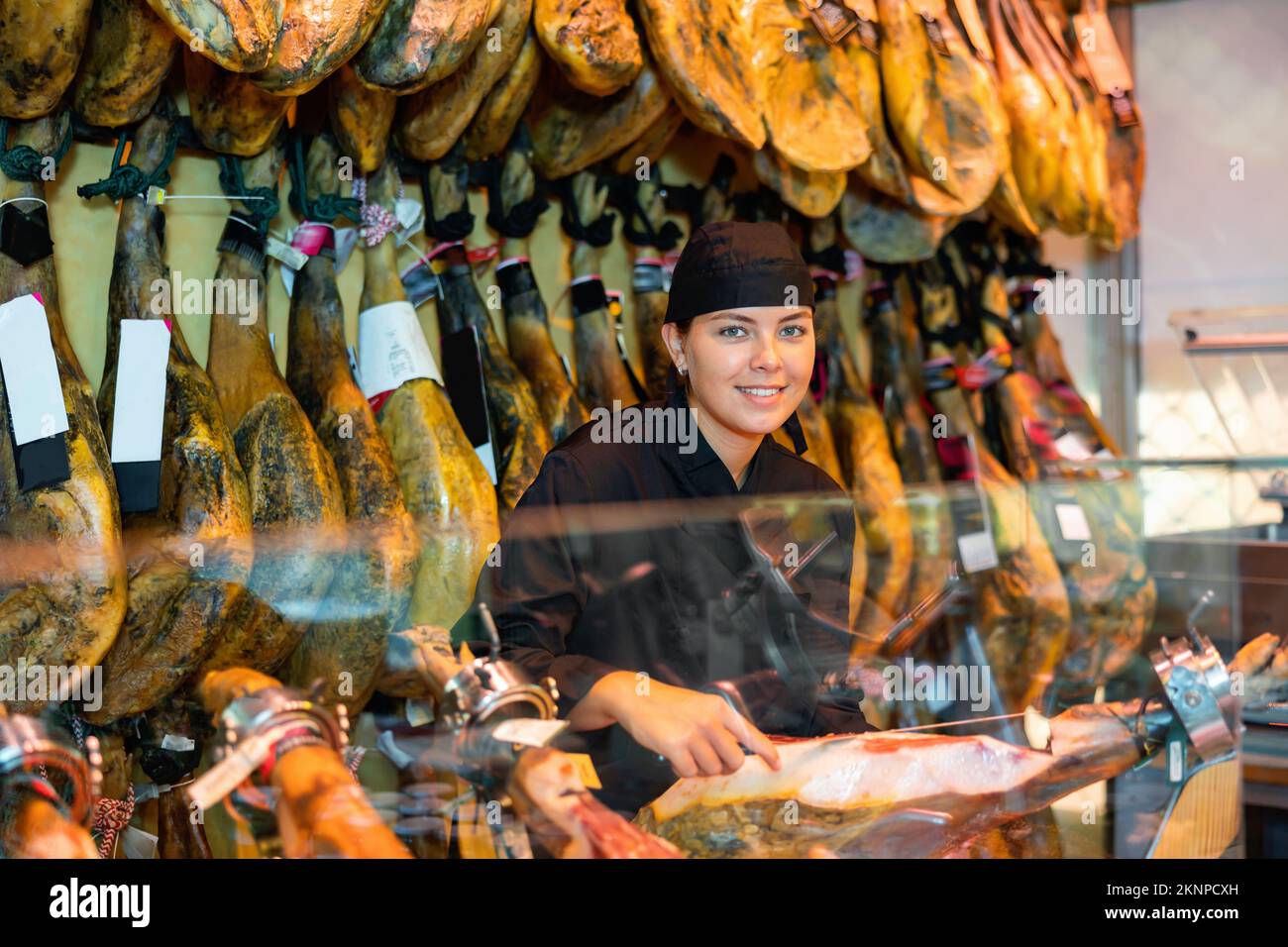 Cheerful young woman cutting ham in jamoneria Stock Photo - Alamy