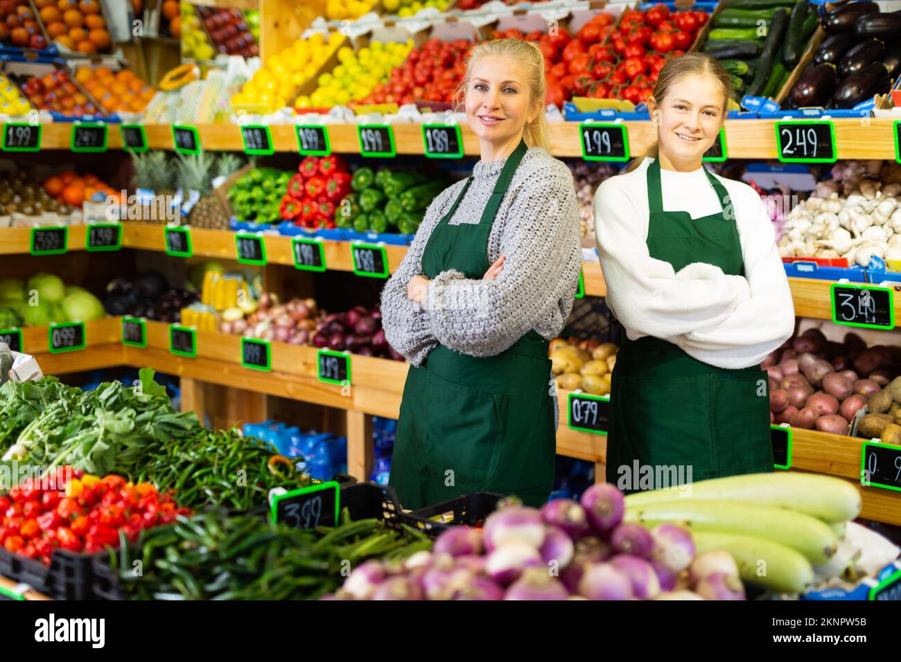 Confident female owner of greengrocery store posing with teen daughter ...