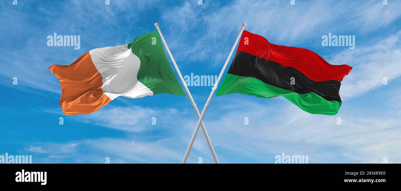two crossed flags Pan-African and Ireland waving in wind at cloudy sky ...