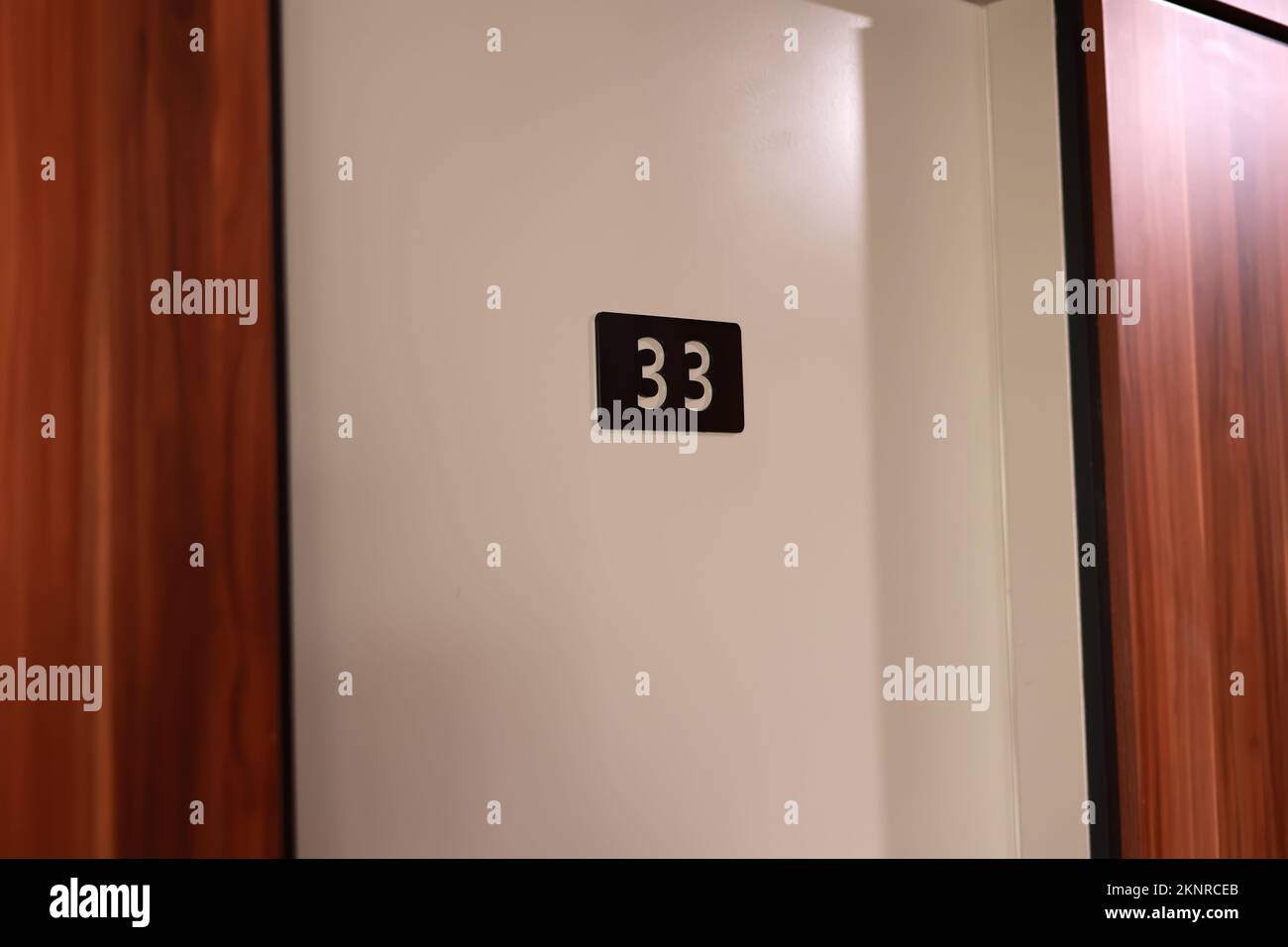 Hotel room 33 number mounted on a white wall. White number on black ...