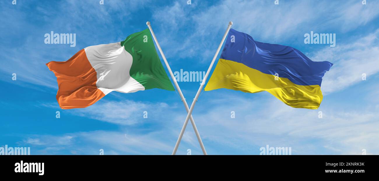two crossed flags Ukraine and Ireland waving in wind at cloudy sky ...