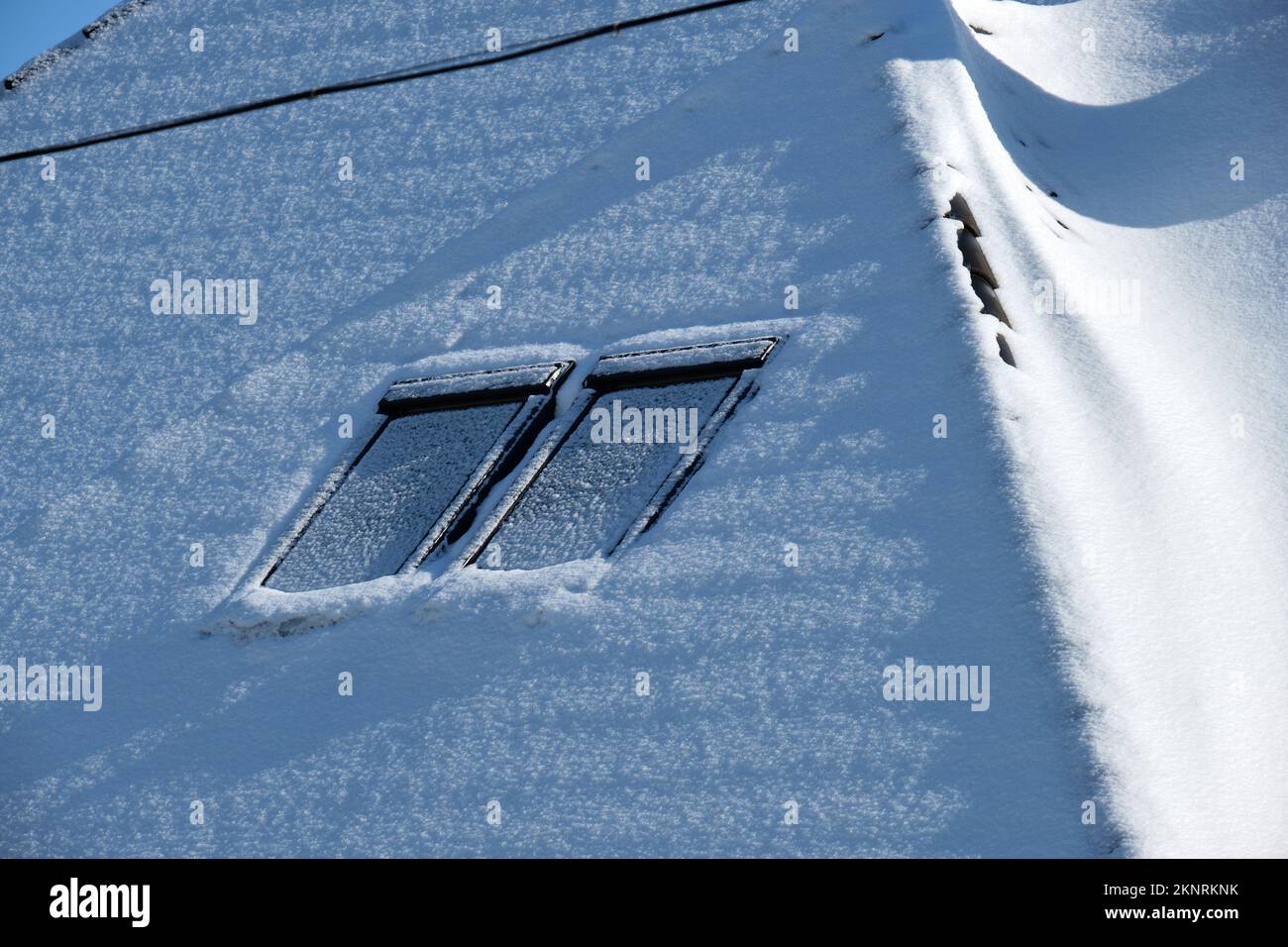 Closeup of house roof top with attic windows covered with snow in cold ...