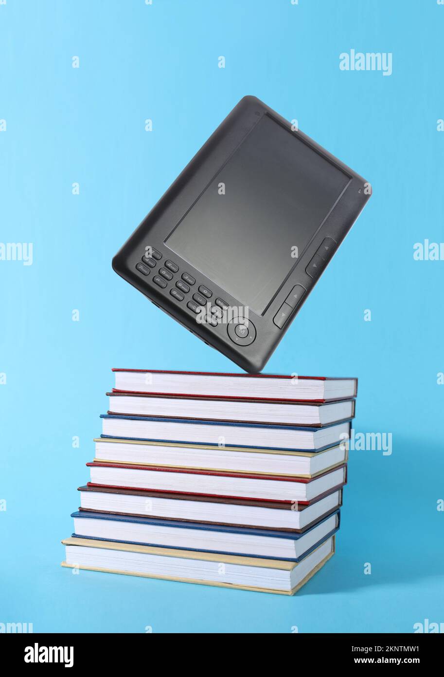 Modern e-reader and stack of books on light blue background Stock Photo ...