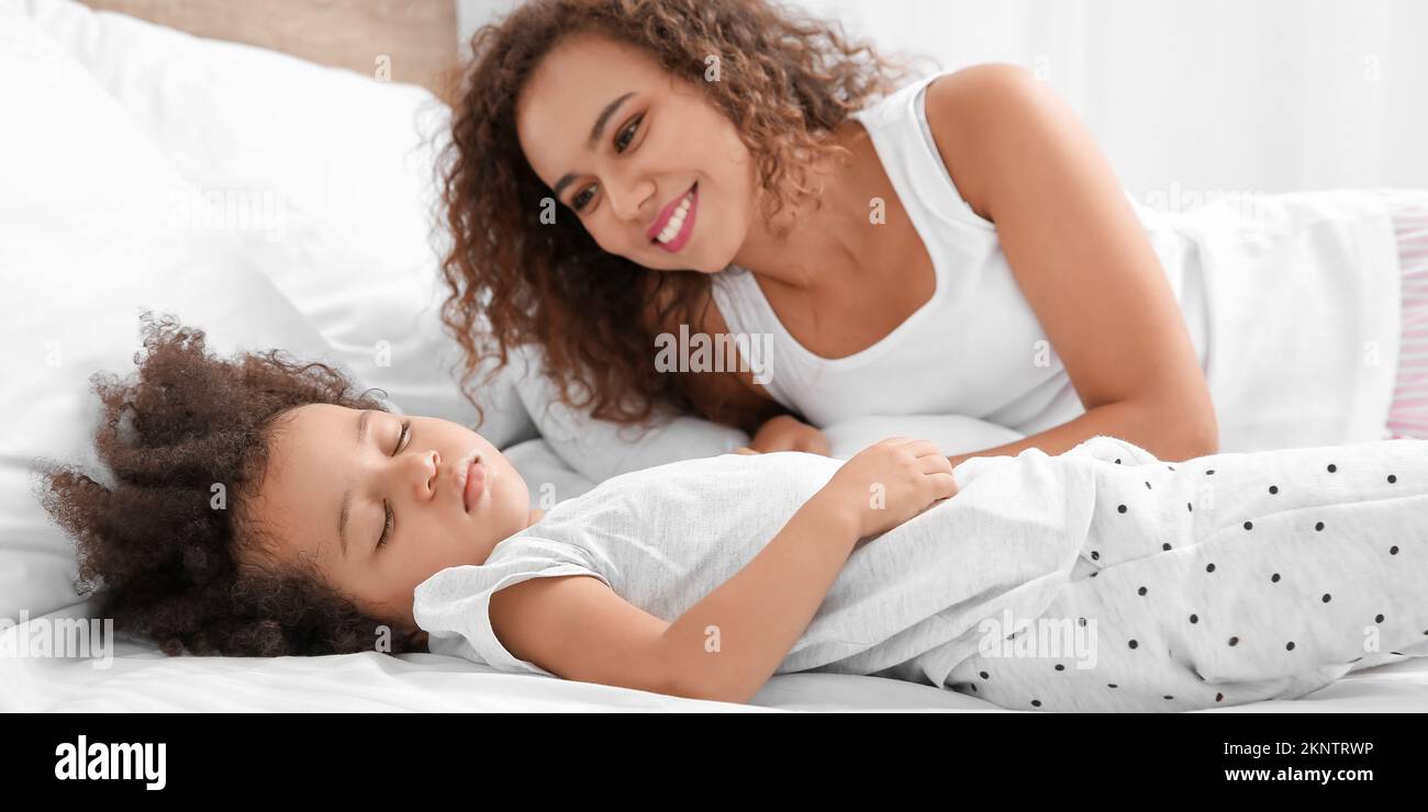 African-American mother with her sleeping daughter lying on bed Stock ...