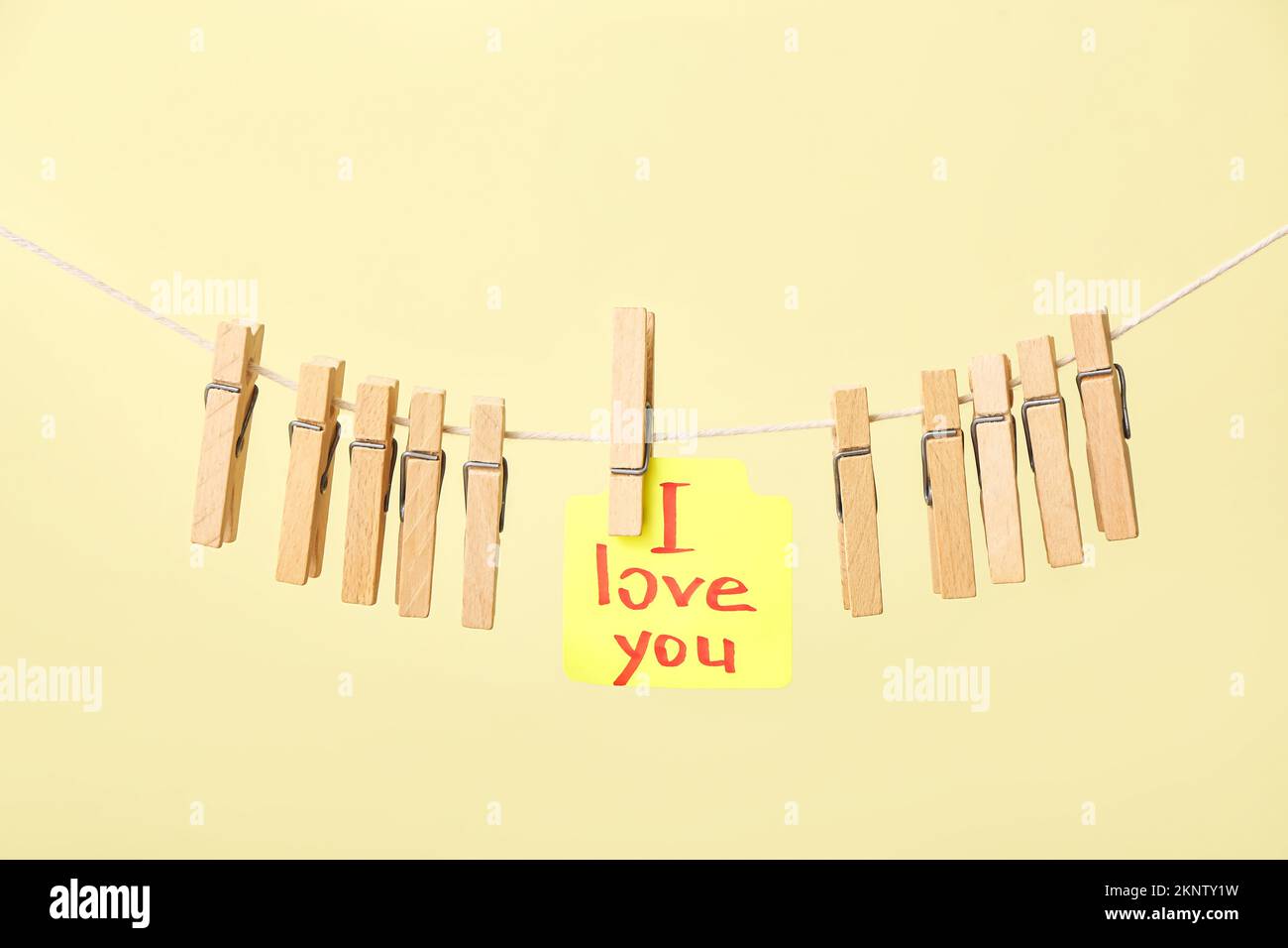 Wooden clothespins and sticky note with text I LOVE YOU hanging on rope ...