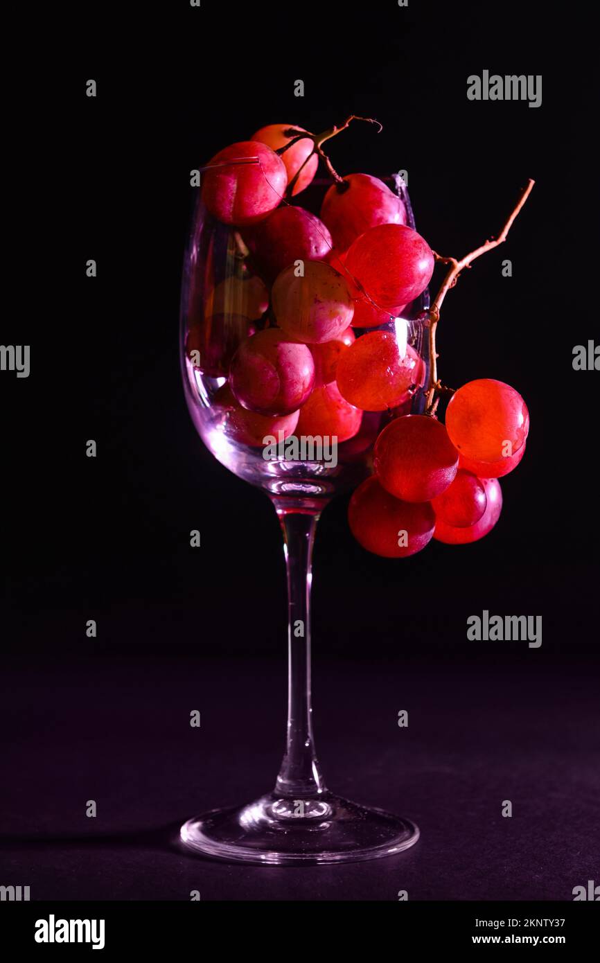 Broken glass with delicious grapes on table against dark background ...