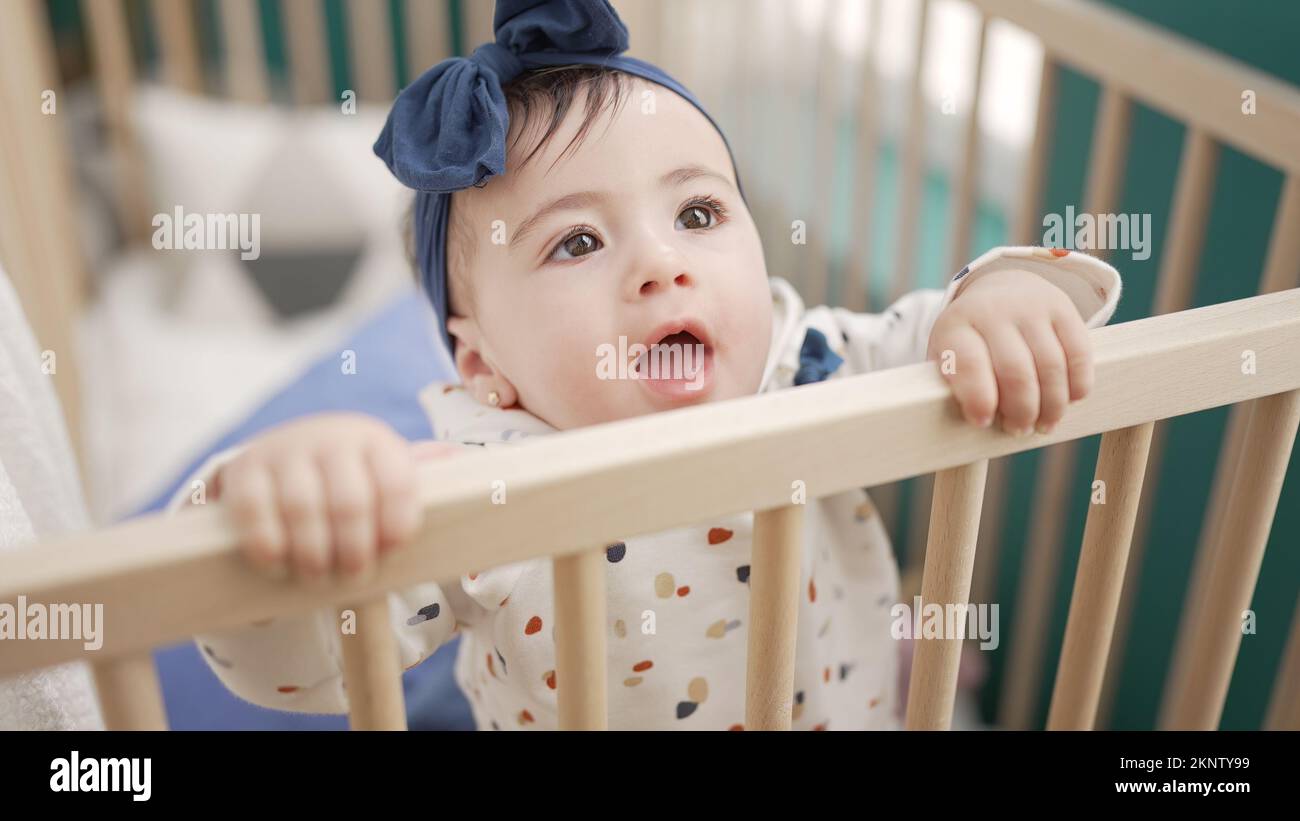 Adorable toddler standing on cradle with relaxed expression at bedroom ...