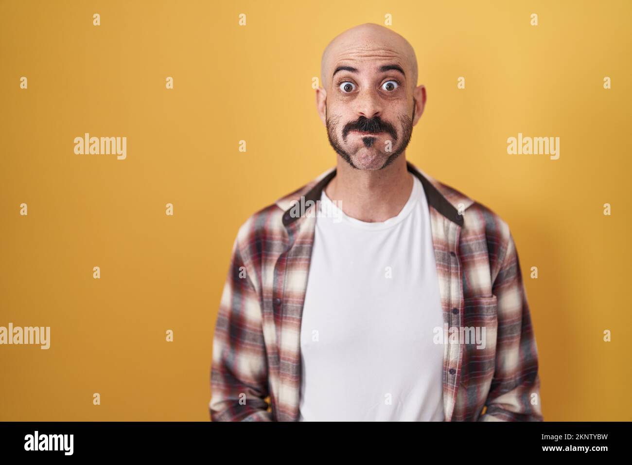 Hispanic man with beard standing over yellow background puffing cheeks ...