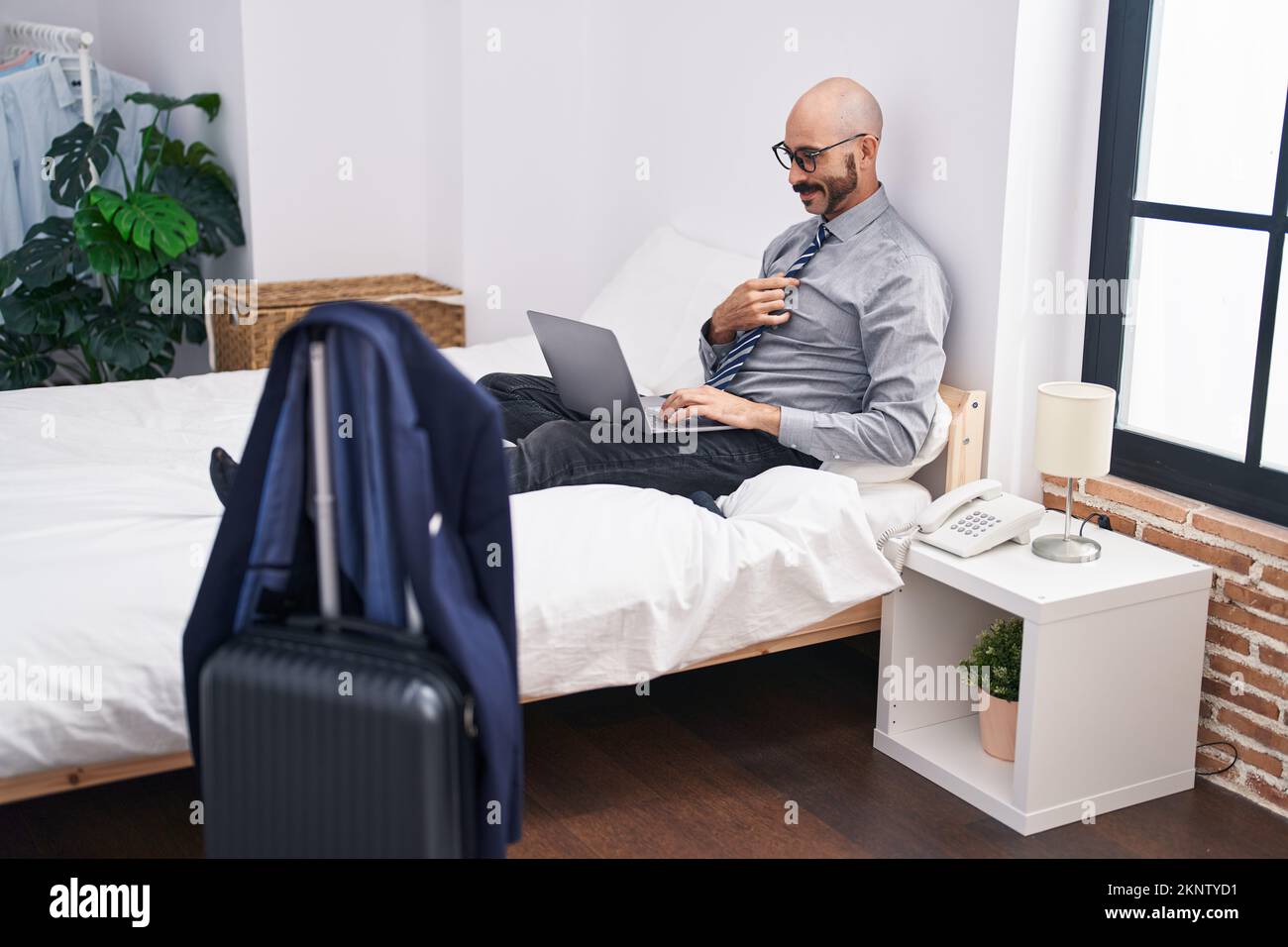 Young hispanic man business worker using laptop sitting on bed at hotel ...