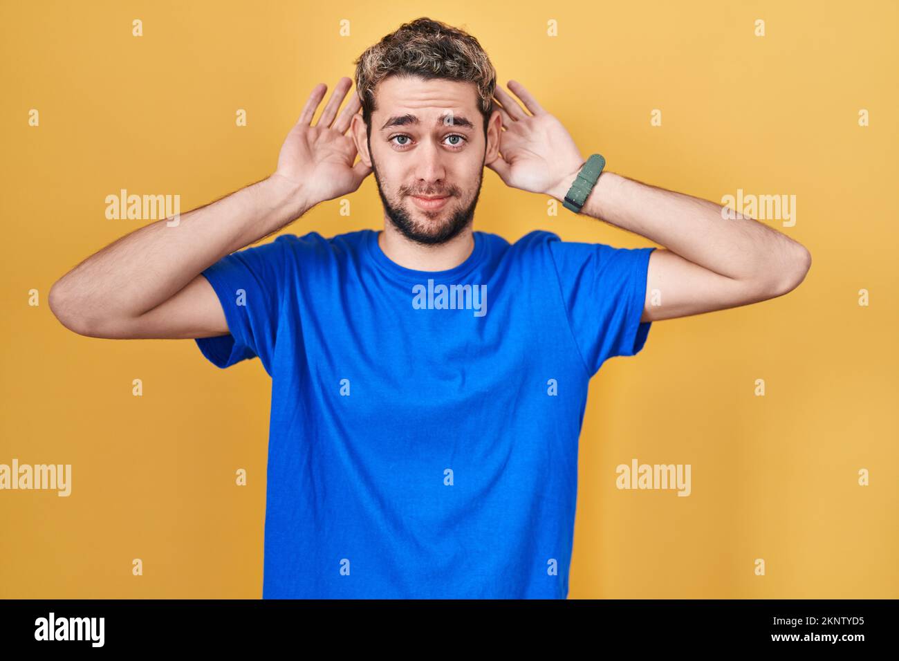 Hispanic man with beard standing over yellow background trying to hear ...