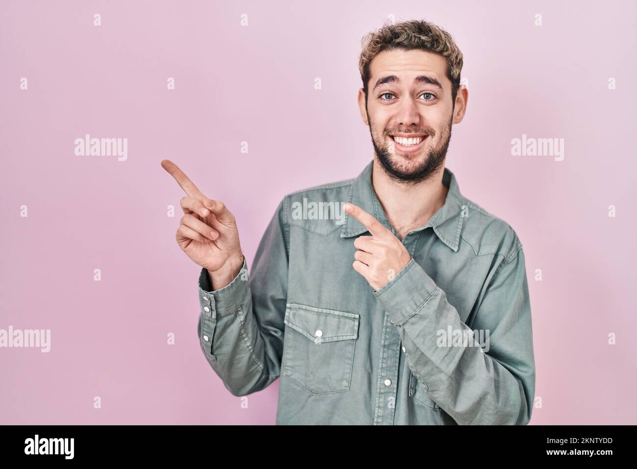 Hispanic man with beard standing over pink background smiling and ...