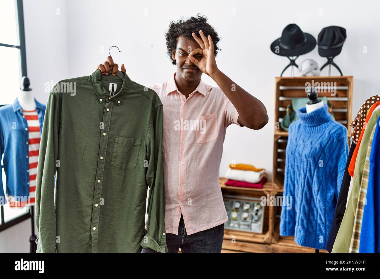 African man with curly hair holding shirt from clothing rack at retail ...