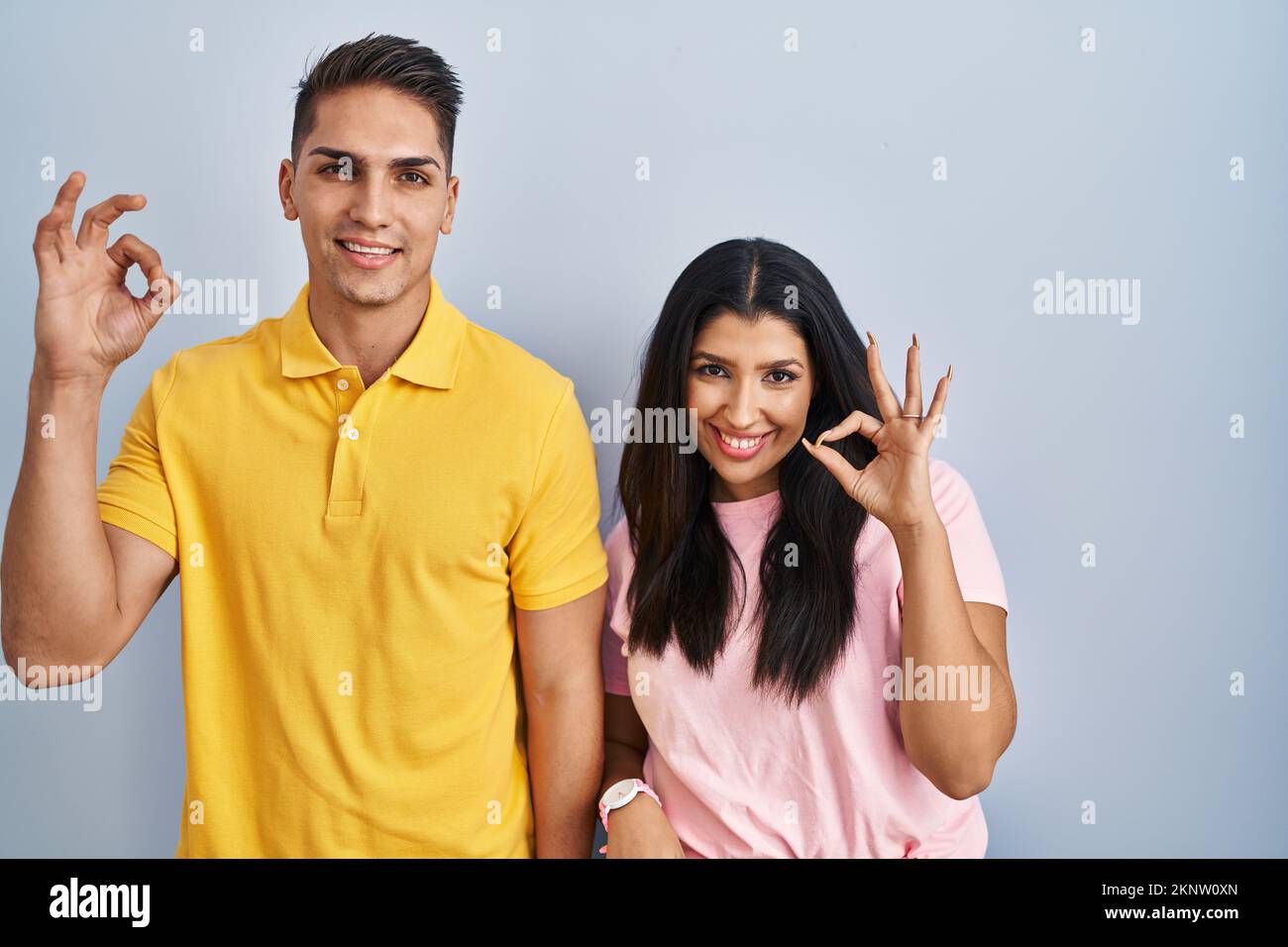 Young couple standing over isolated background smiling positive doing ...