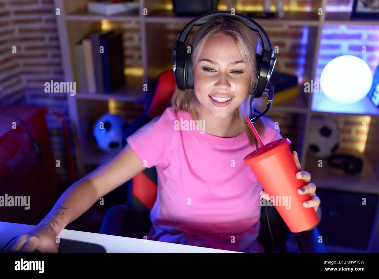 Young blonde woman streamer playing video game drinking beverage at ...