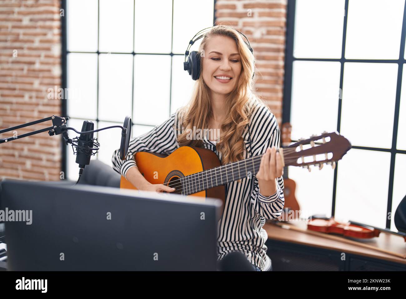 Young blonde woman musician playing classical guitar at music studio ...