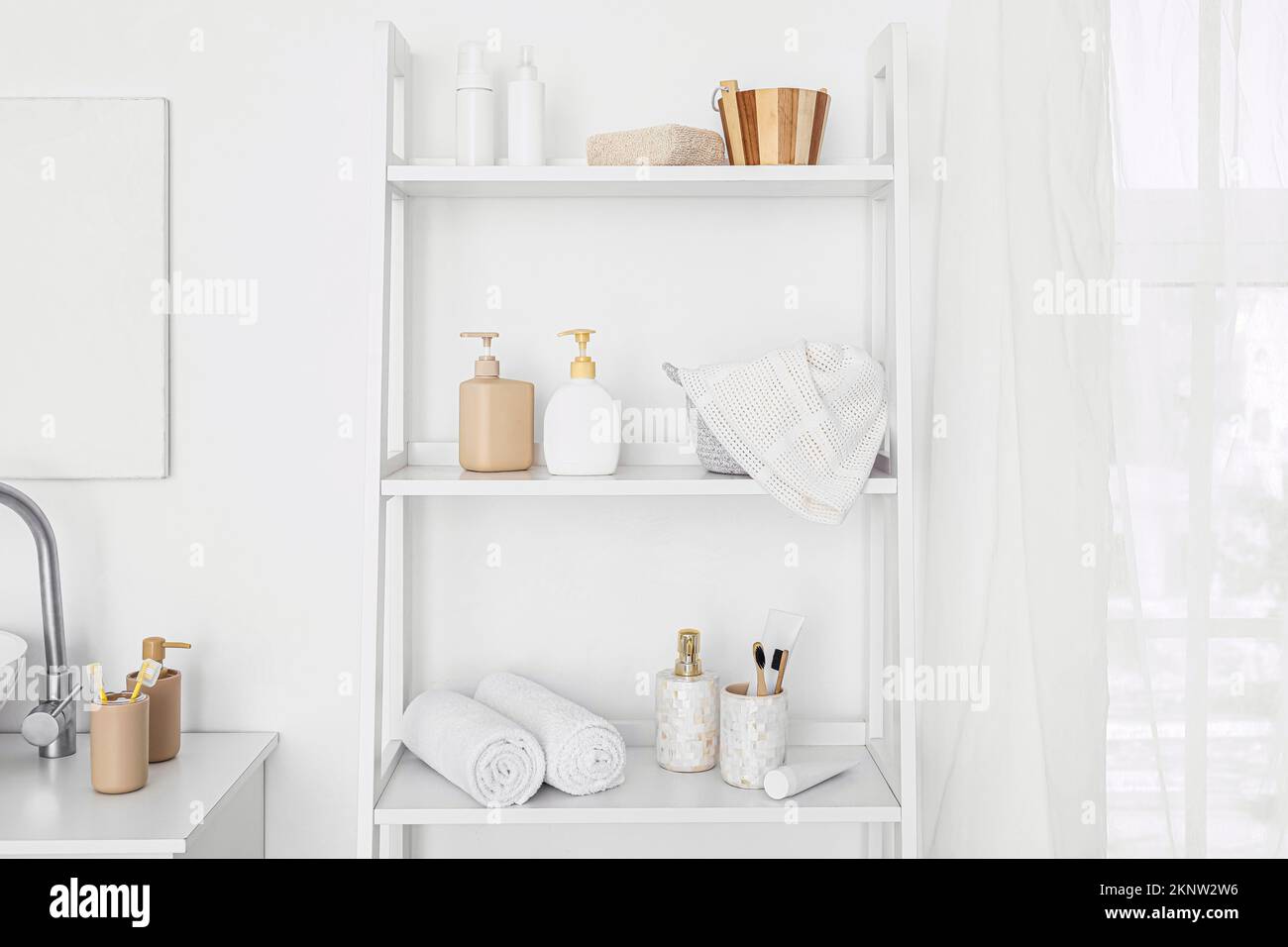 Shelf unit with bath accessories near white wall in bathroom Stock ...