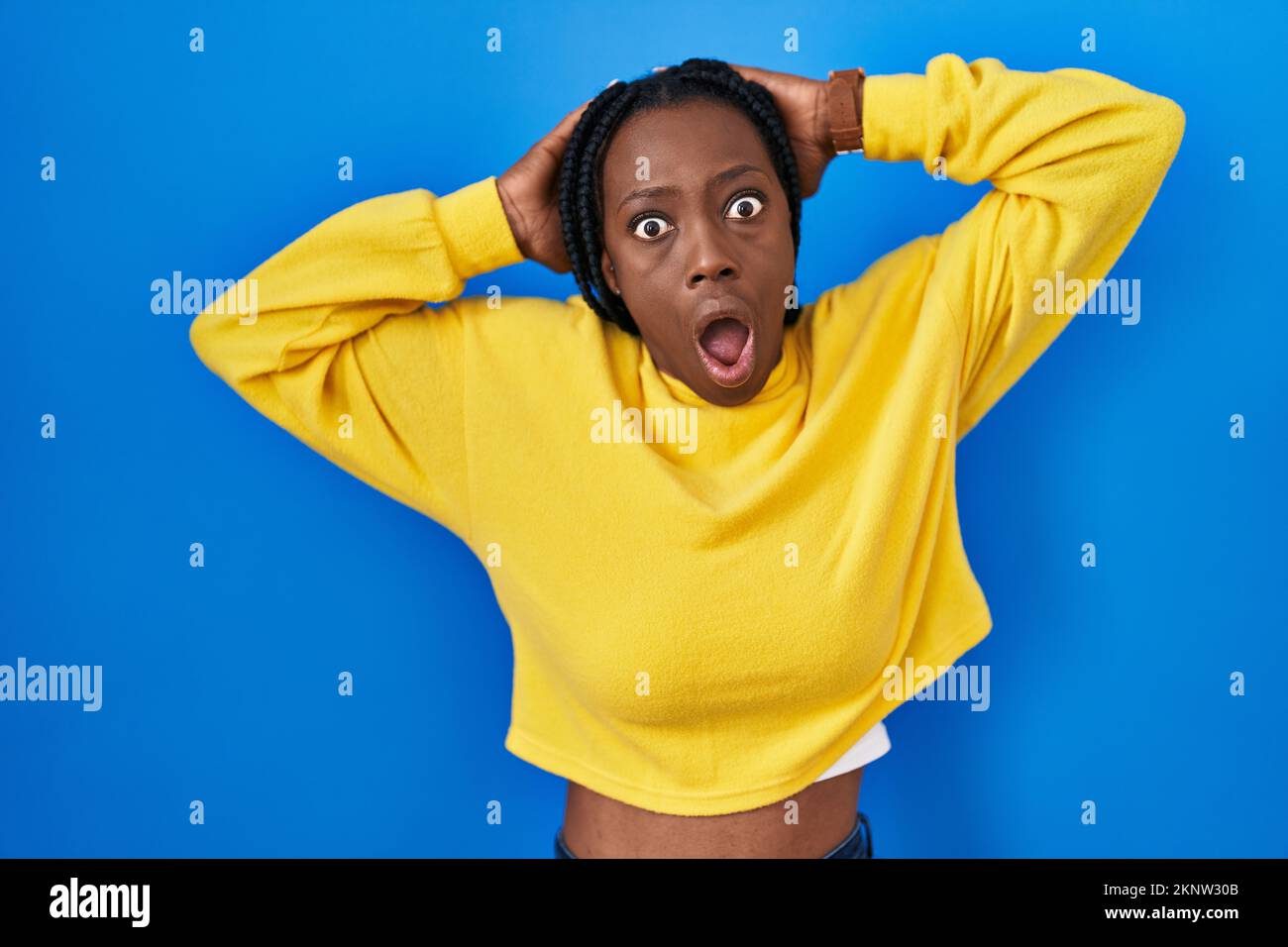 Beautiful black woman standing over blue background crazy and scared ...