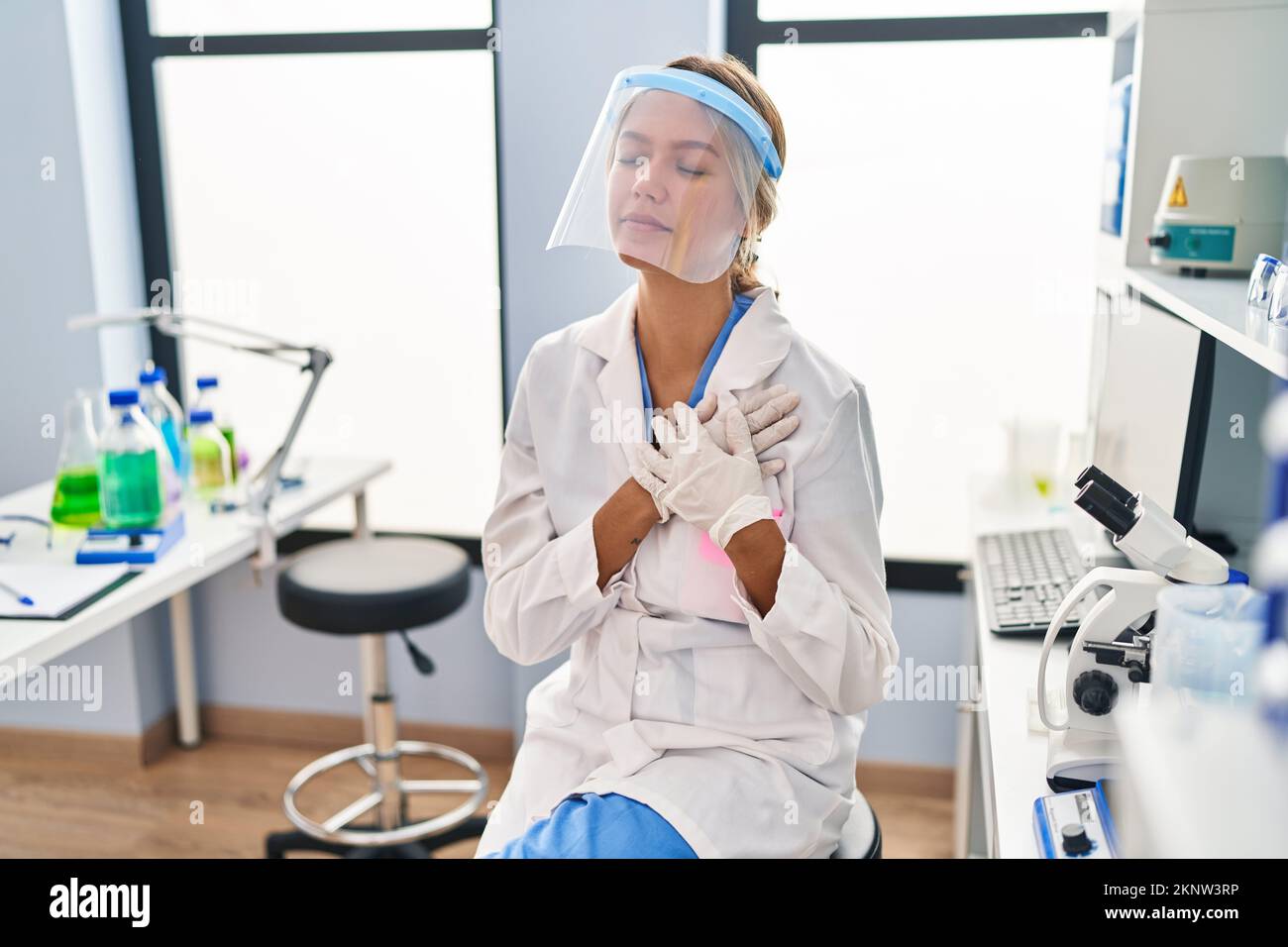 Young blonde woman working at scientist laboratory wearing face mask ...