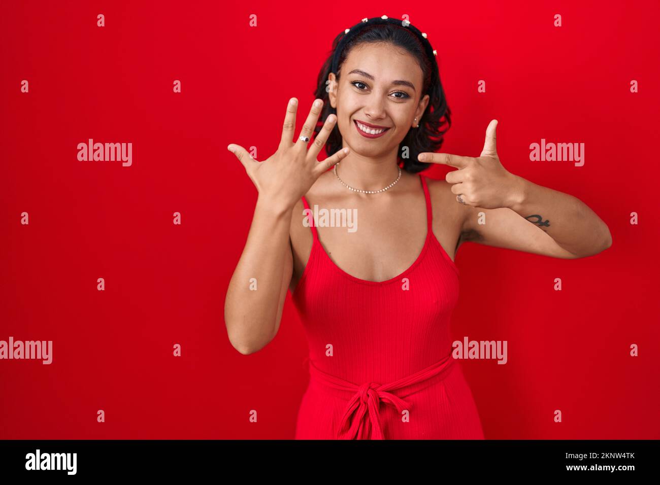 Young hispanic woman standing over red background showing and pointing ...