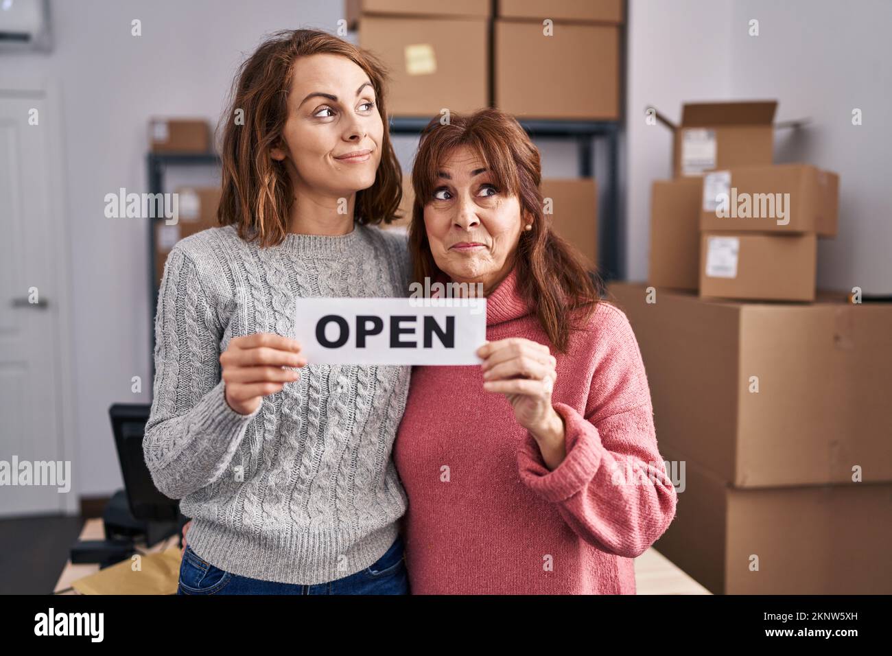 Two women working at small business ecommerce holding open banner ...