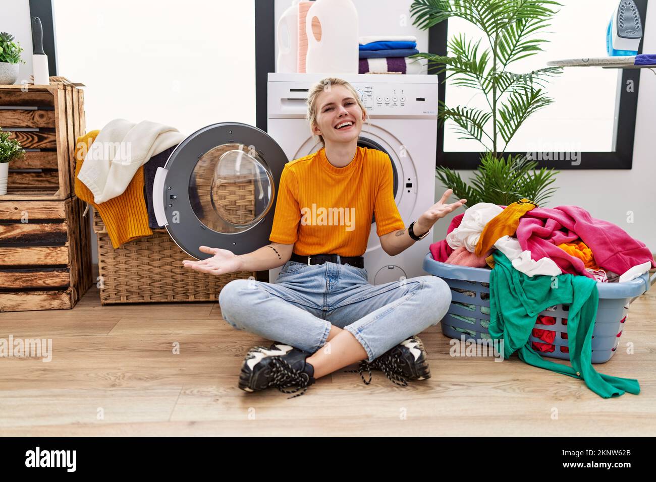 Young blonde woman doing laundry sitting by washing machine smiling ...