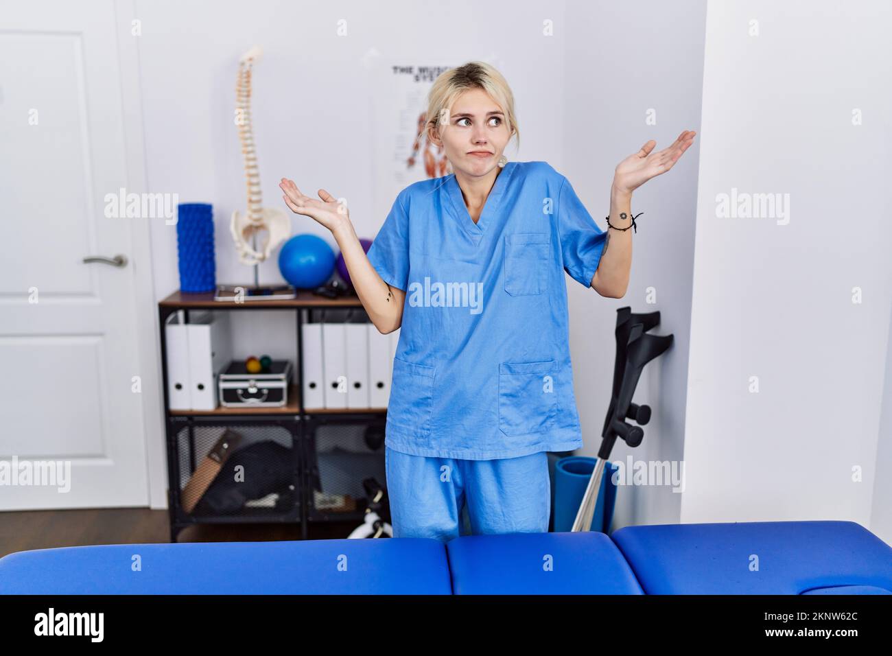 Young physiotherapist woman working at pain recovery clinic clueless ...