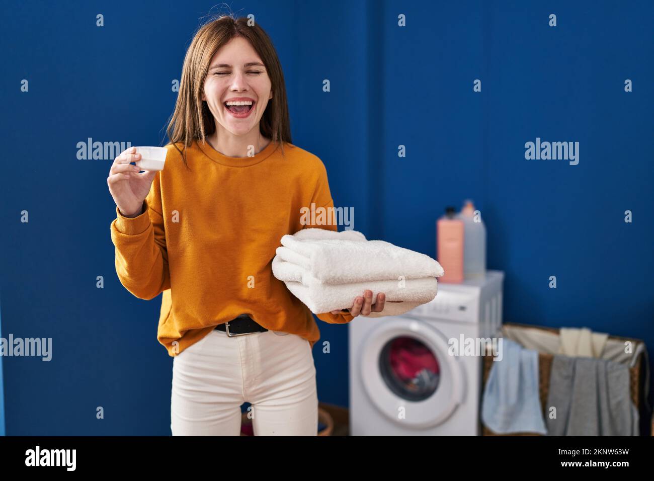 Young brunette woman holding detergent and clean laundry smiling and ...
