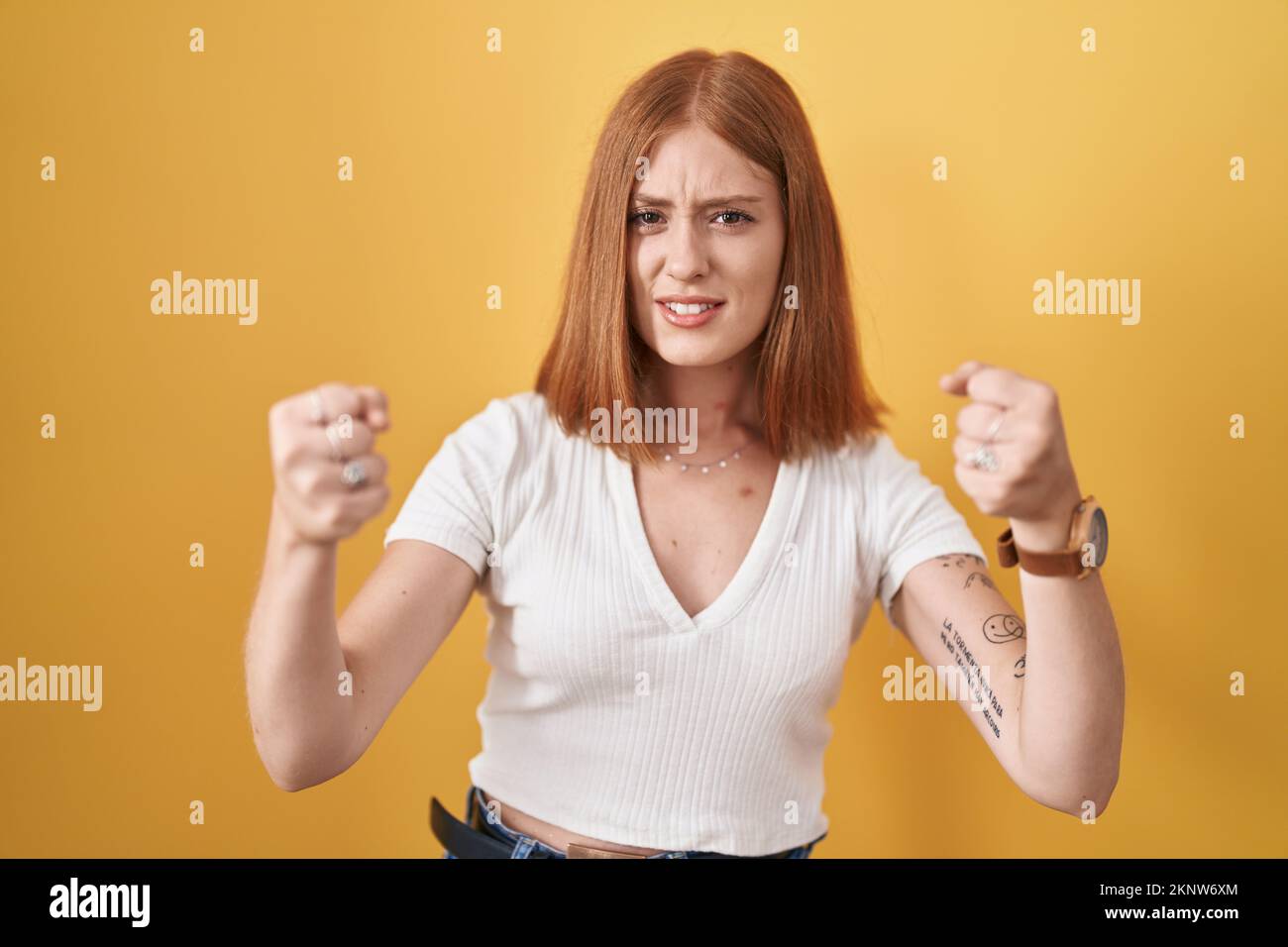 Young redhead woman standing over yellow background angry and mad ...