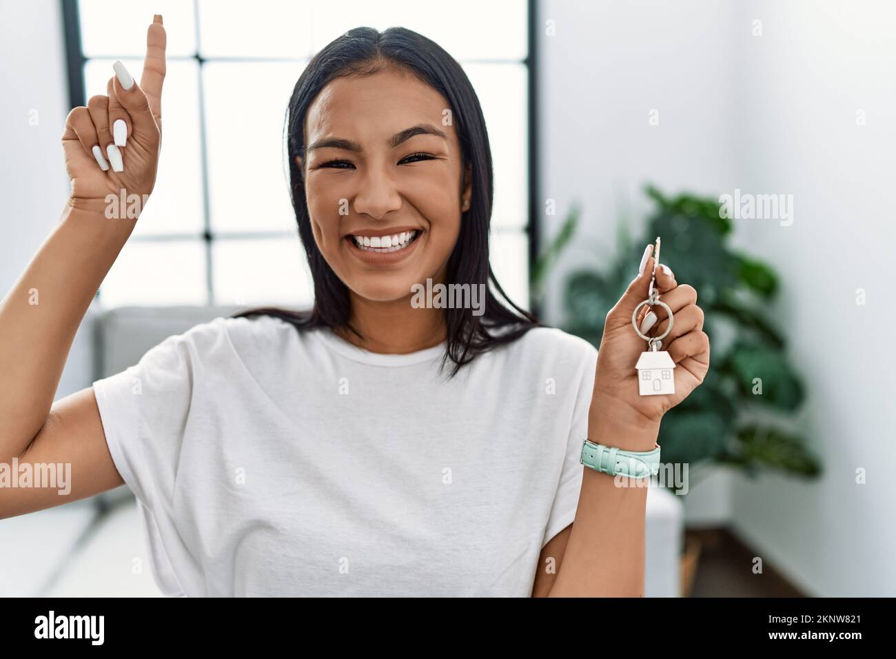 Young hispanic woman holding keys of new home smiling amazed and surprised and pointing up with ...