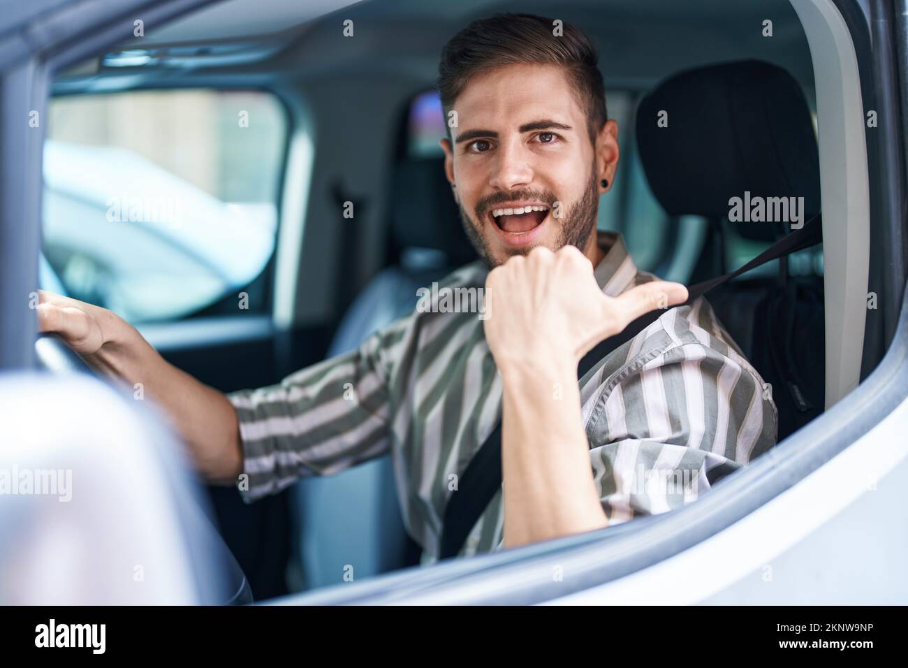 Hispanic man with beard driving car pointing thumb up to the side ...