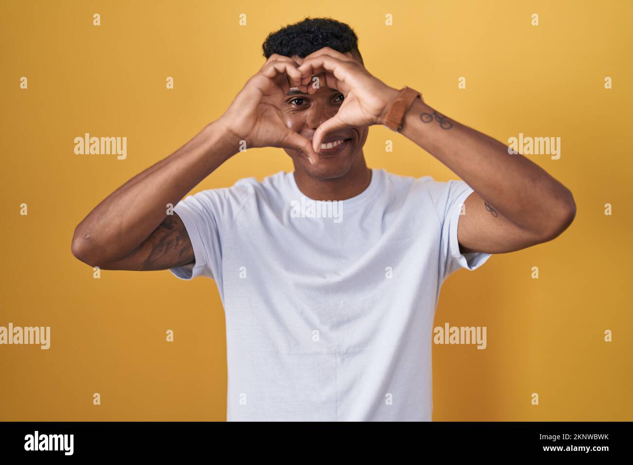 Young hispanic man standing over yellow background doing heart shape ...