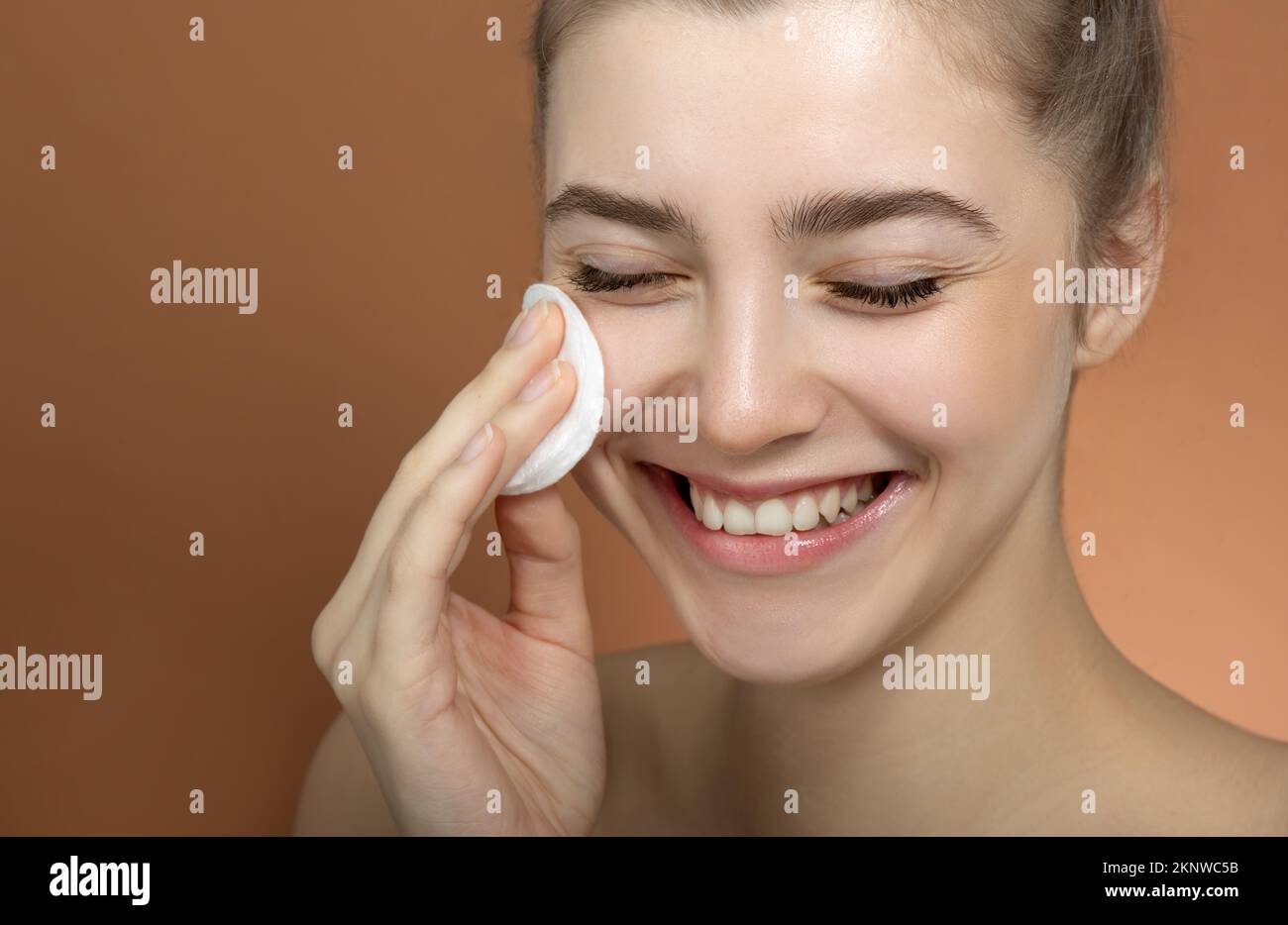 Beauty model cleansing her perfect skin with a cotton pad sponge, close-up. A young woman cares ...