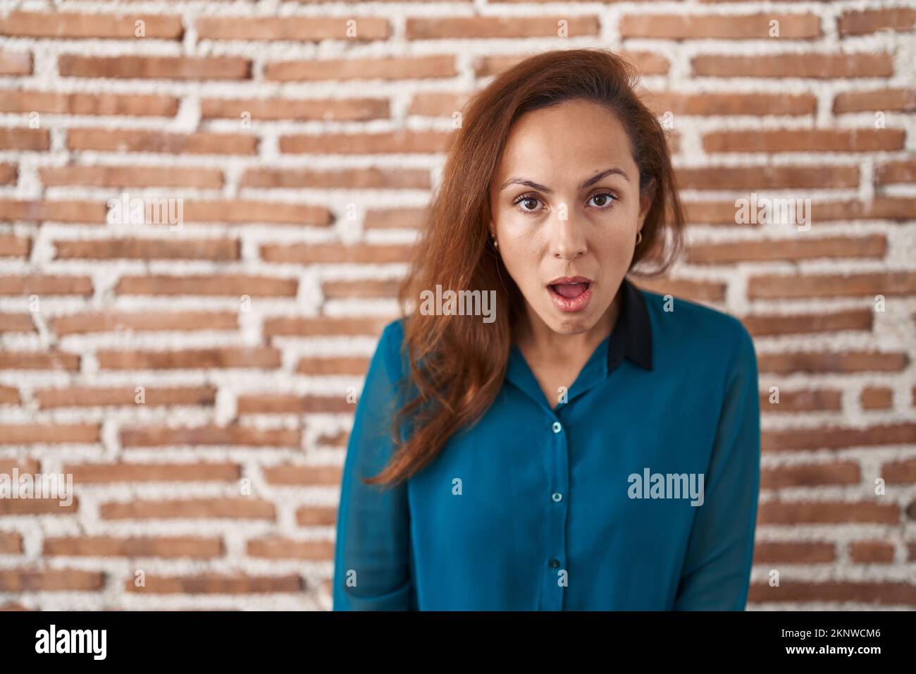 Brunette Woman Standing Over Bricks Wall Afraid And Shocked With