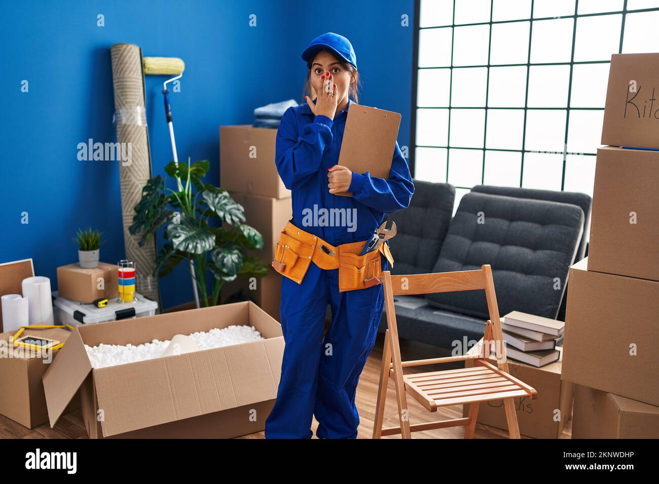 Young hispanic technician working at house renovation covering mouth ...