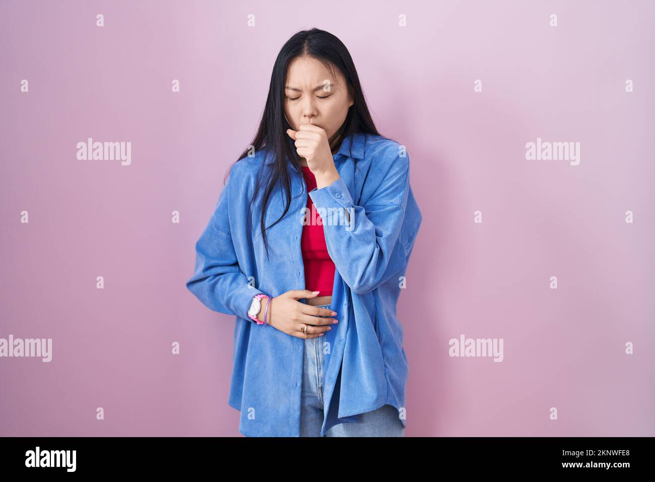 Young asian woman standing over pink background feeling unwell and ...