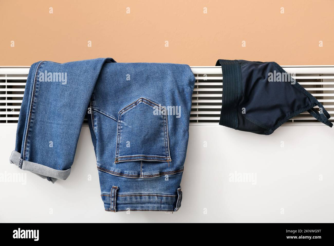 Sports bra and jeans drying on electric radiator near beige wall ...