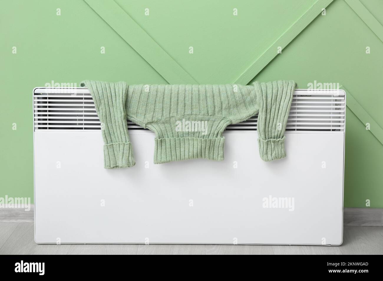 Warm sweater drying on electric radiator near green wall Stock Photo ...