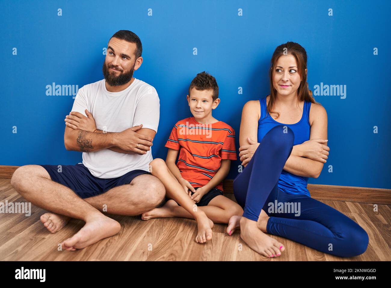 Family of three sitting on the floor at home smiling looking to the ...