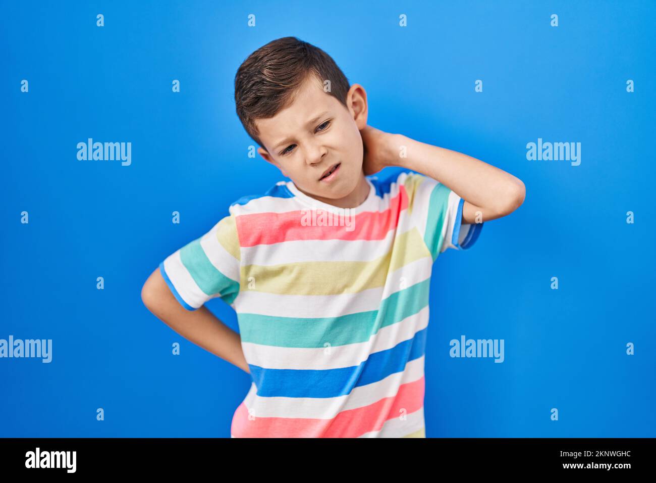 Young caucasian kid standing over blue background suffering of neck ...