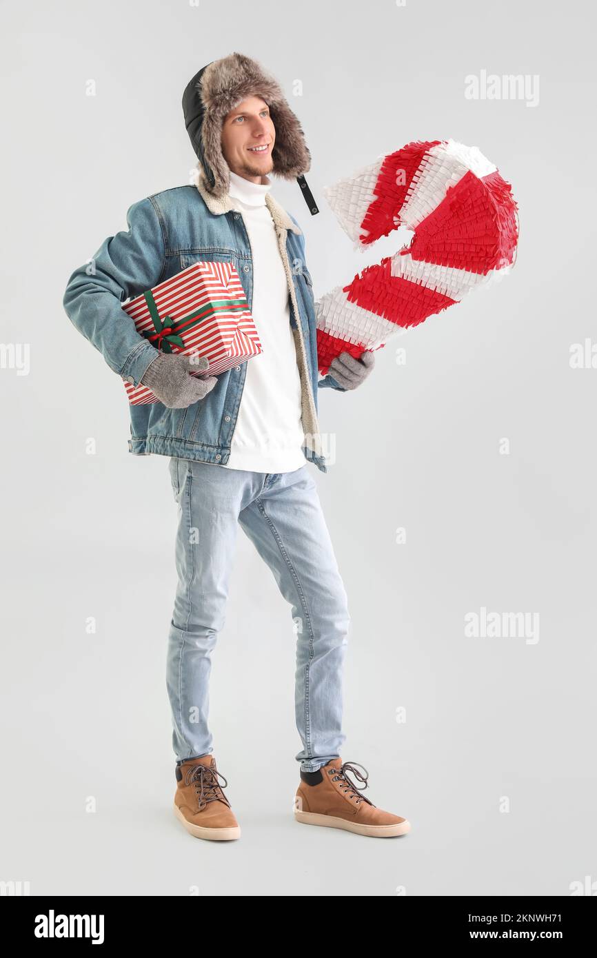 Handsome man with Christmas present and candy cane pinata on light ...