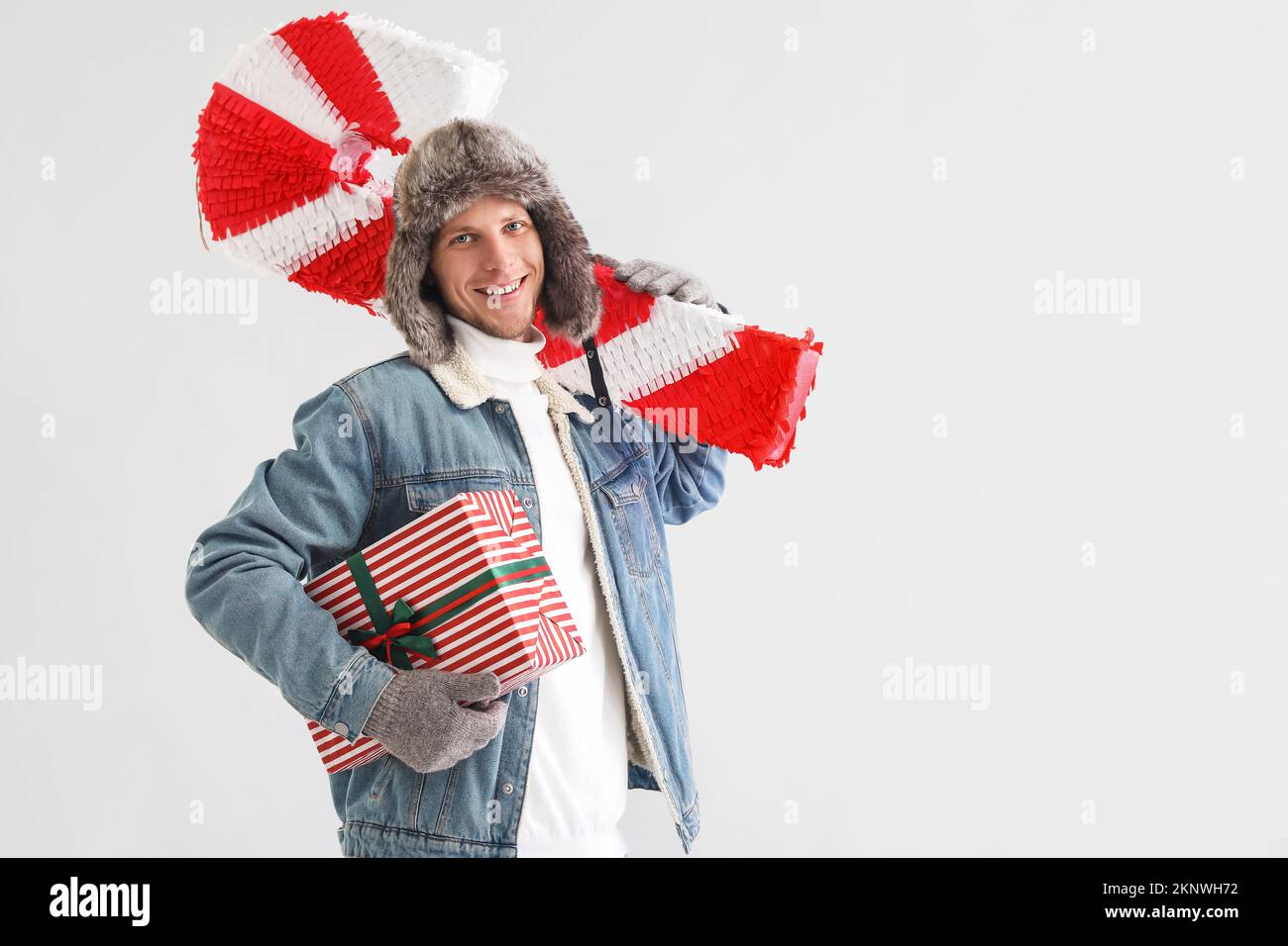 Handsome man with Christmas present and candy cane pinata on light ...