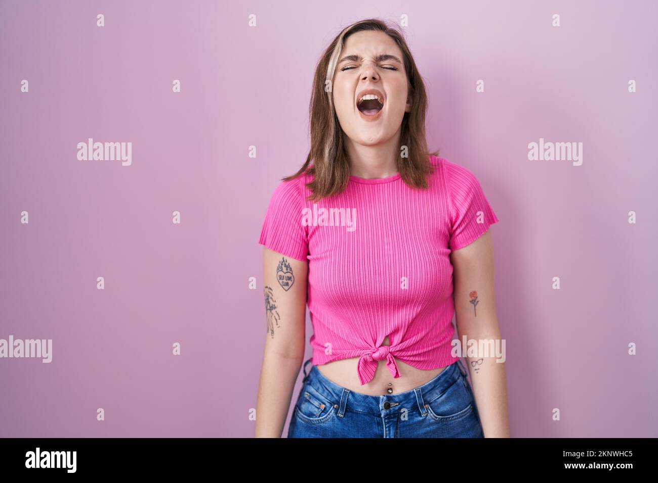 Blonde caucasian woman standing over pink background angry and mad ...