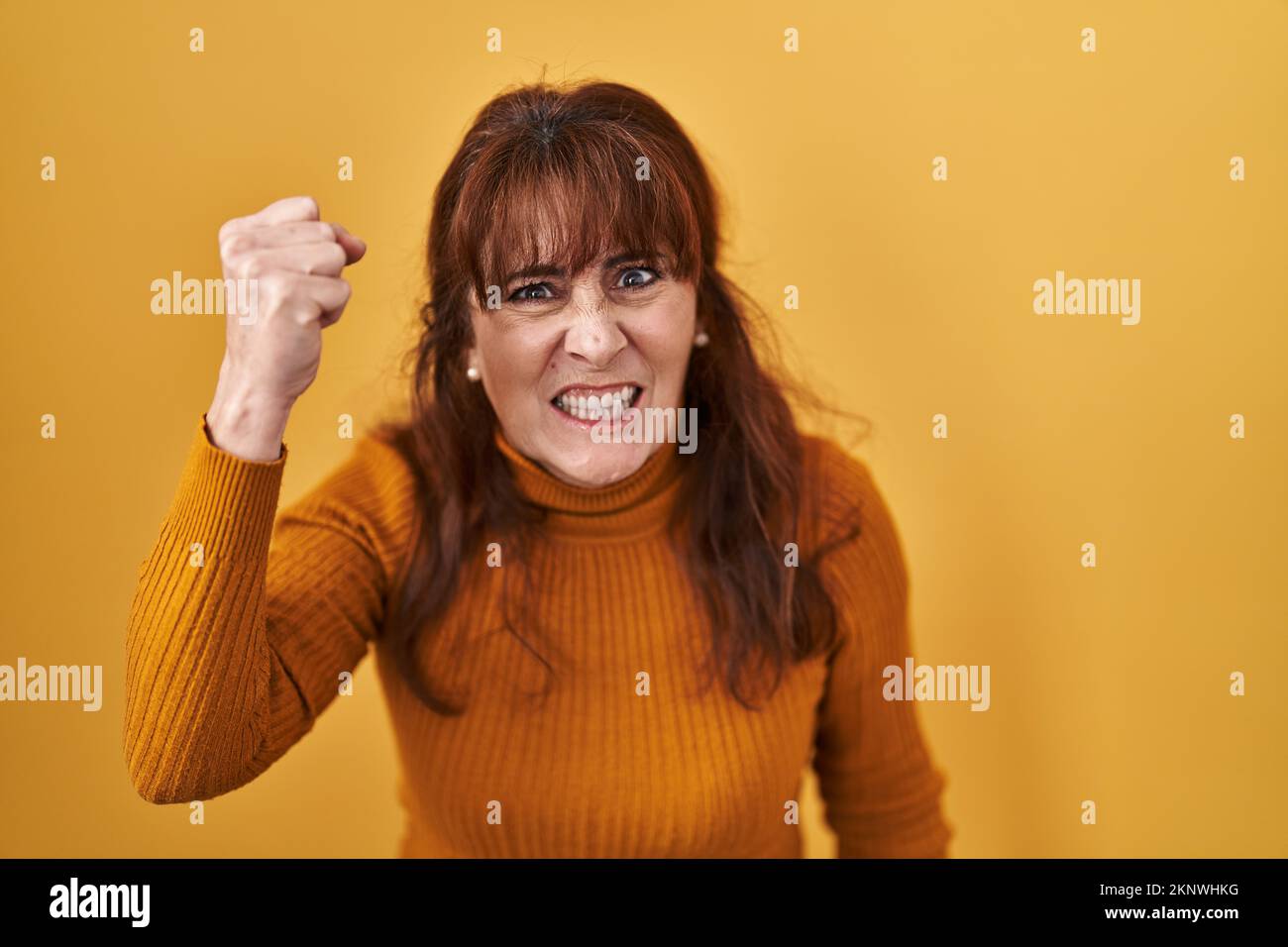 Middle age hispanic woman standing over yellow background angry and mad ...