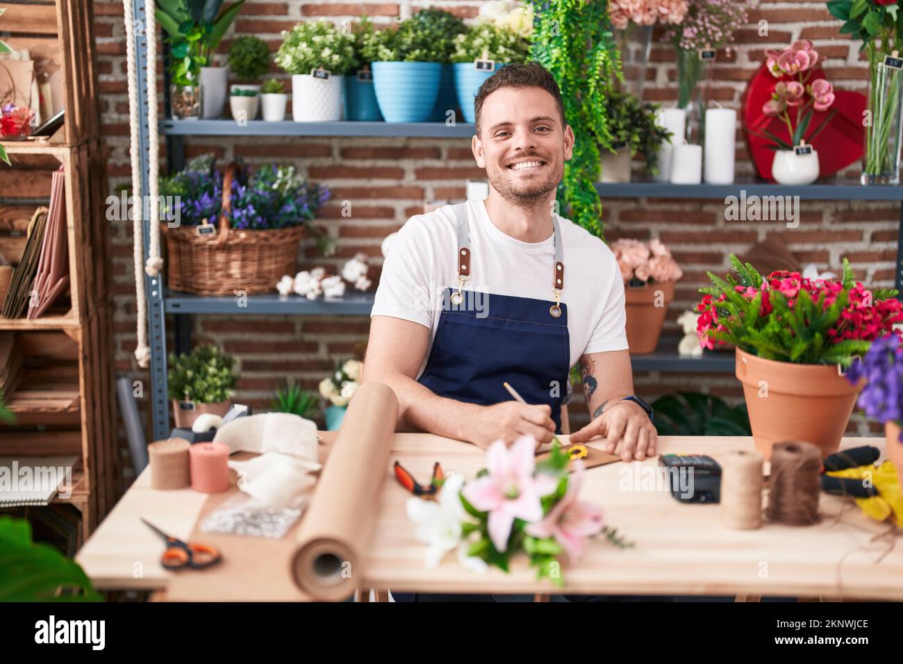 Young hispanic man florist smiling confident writing on envelope letter ...